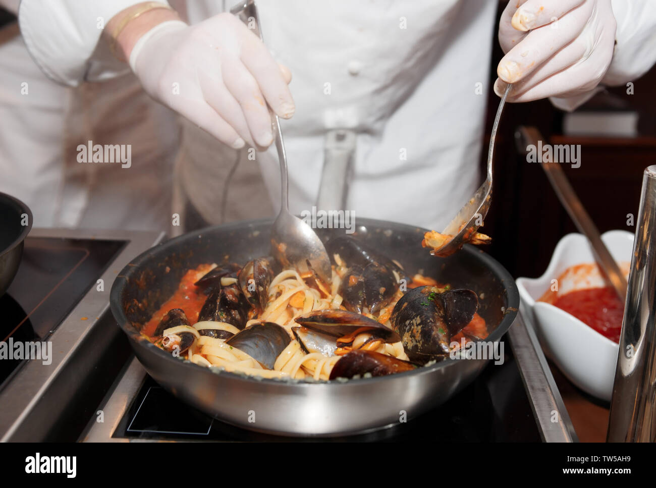 Chef frying mussels with pasta on commercial kitchen in restaurant ...