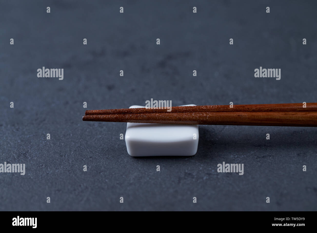 Wooden chopsticks and chopstick rest on black stone background. Close ...