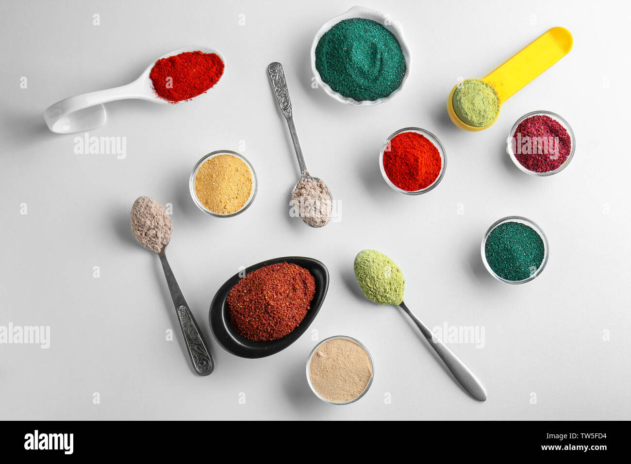 Kitchenware with various colorful superfood powders on white background ...