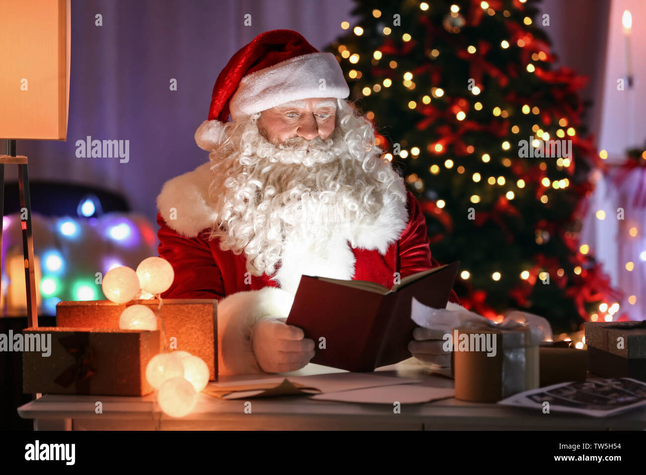 Authentic Santa Claus reading book at table in room decorated for ...