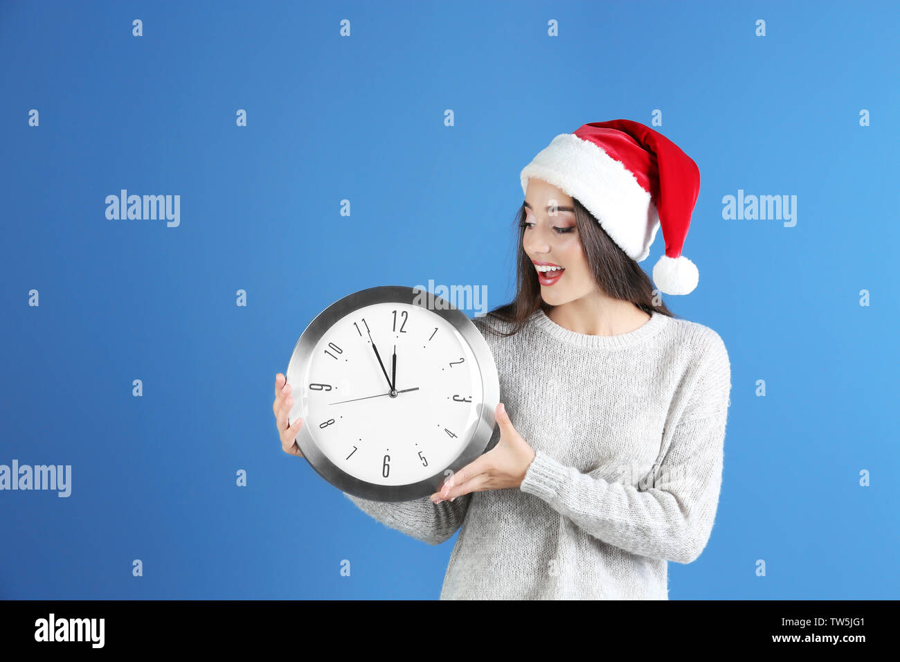 Young woman in Santa hat with clock on color background. Christmas ...