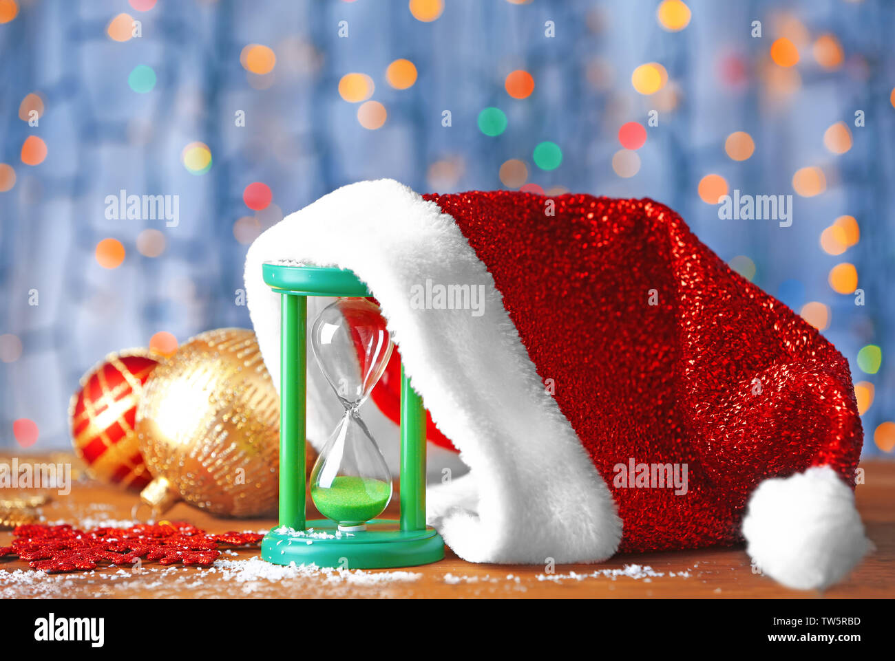 Hourglass with Santa hat and decorations against defocused lights ...