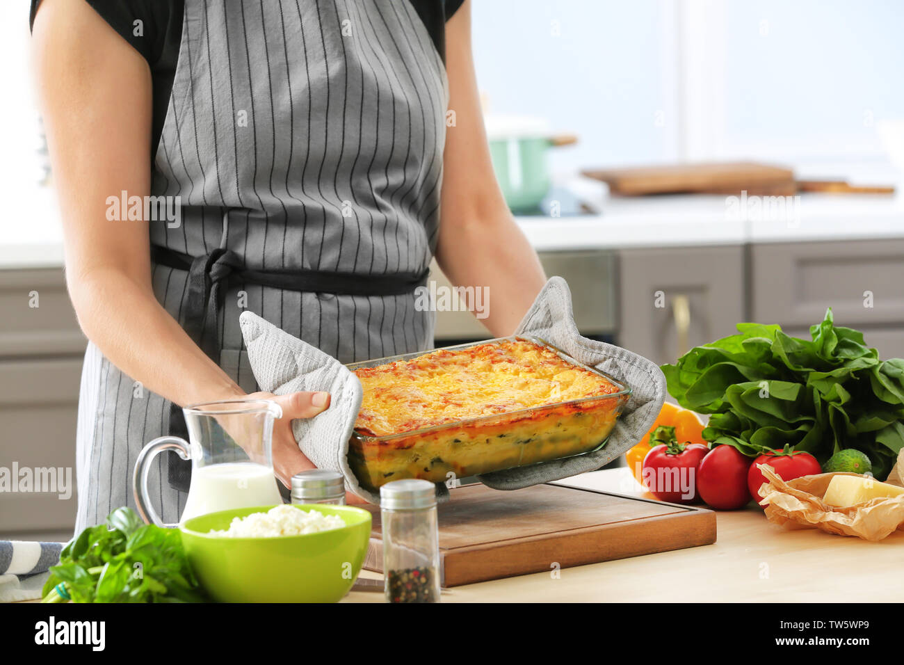 Woman holding baking tray with spinach lasagna in kitchen Stock Photo ...