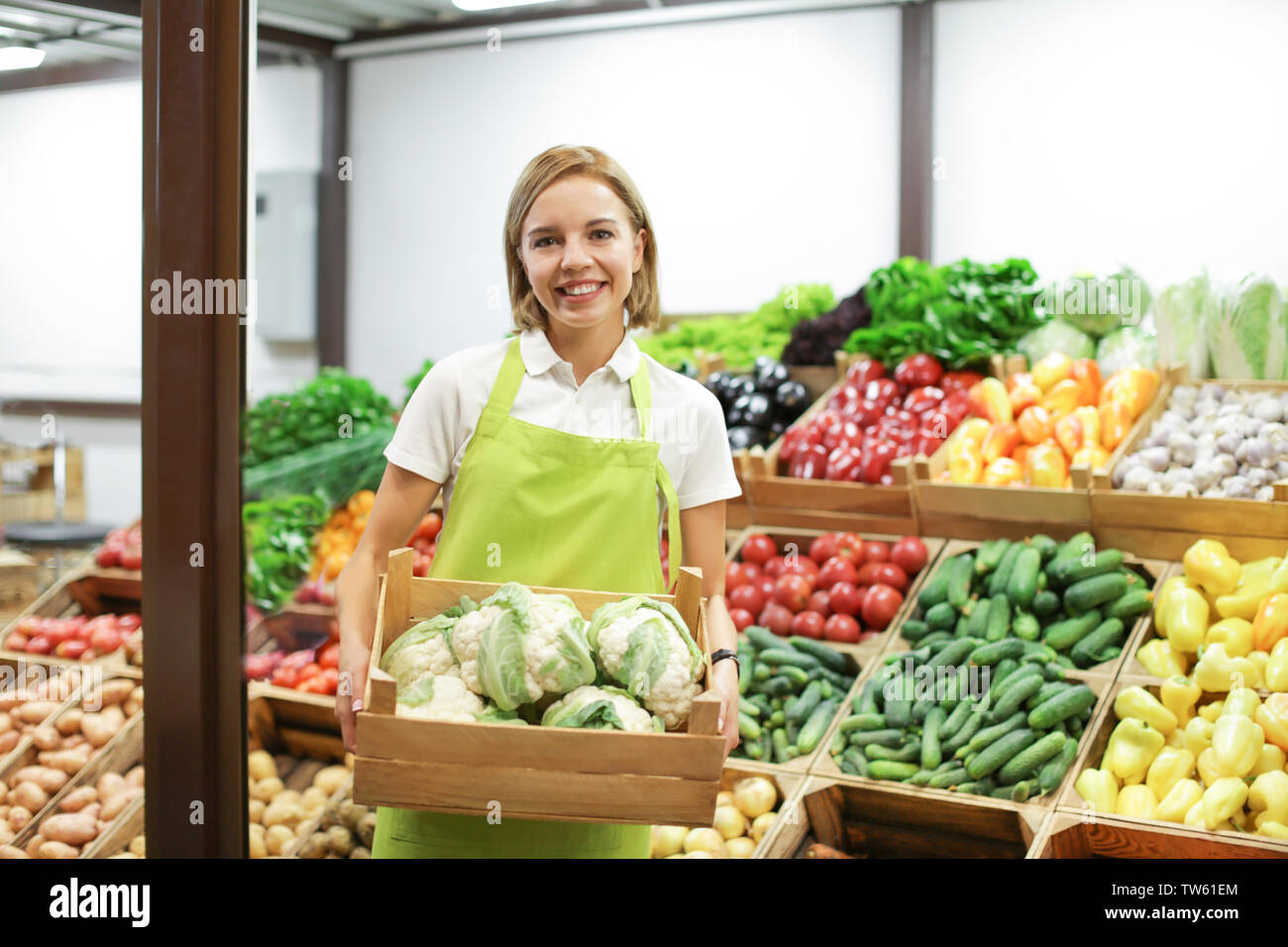Young shop assistant holding wooden crate with cauliflower at market ...