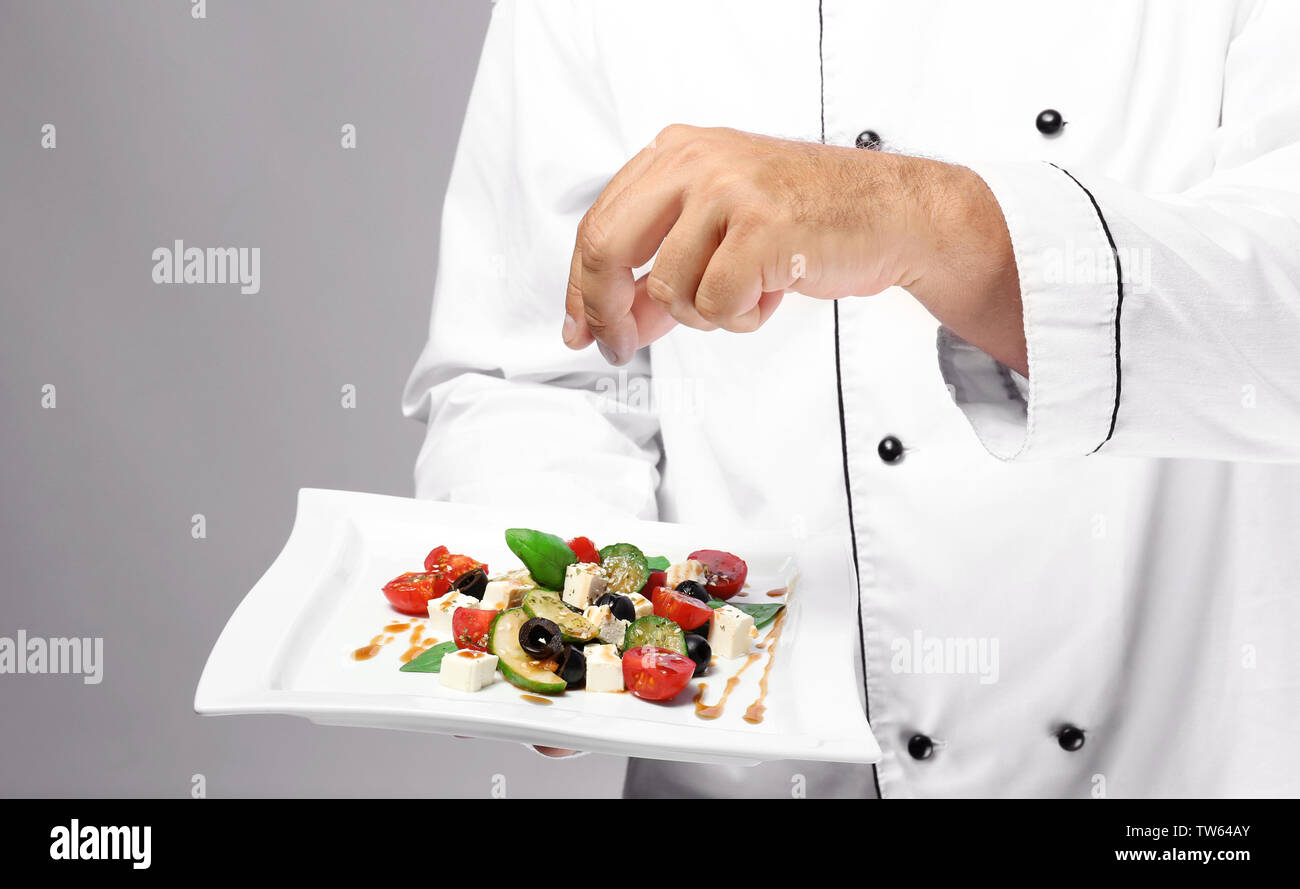 Male chef in uniform adding seasoning to salad on grey background Stock ...