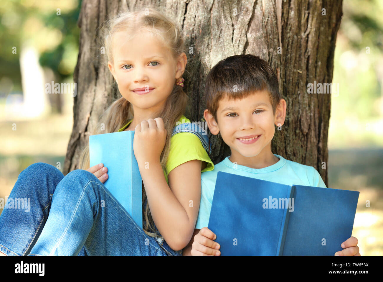 Cute little children reading books near tree in park Stock Photo - Alamy