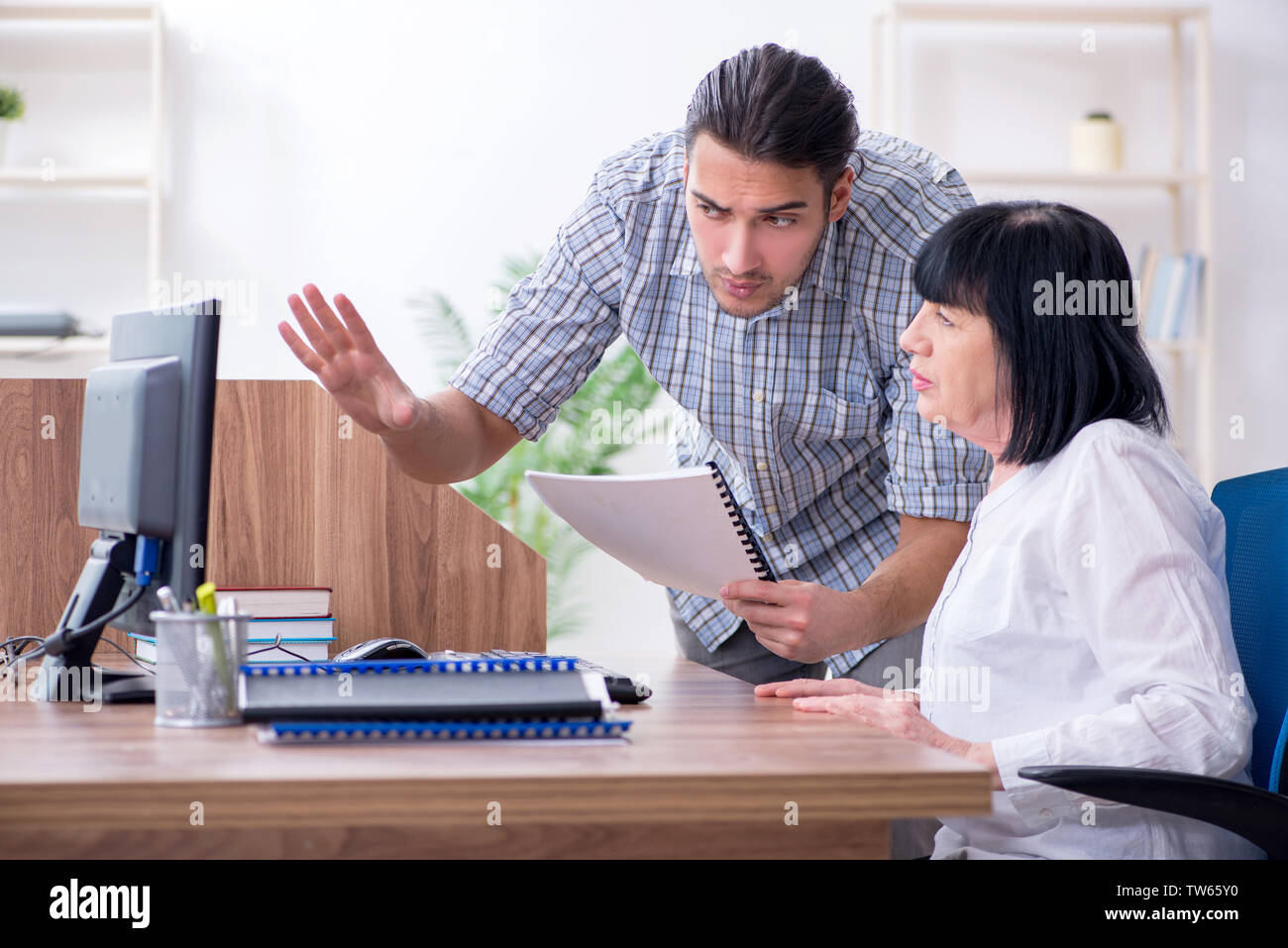 Young male employee explaining to old female colleague how to use ...