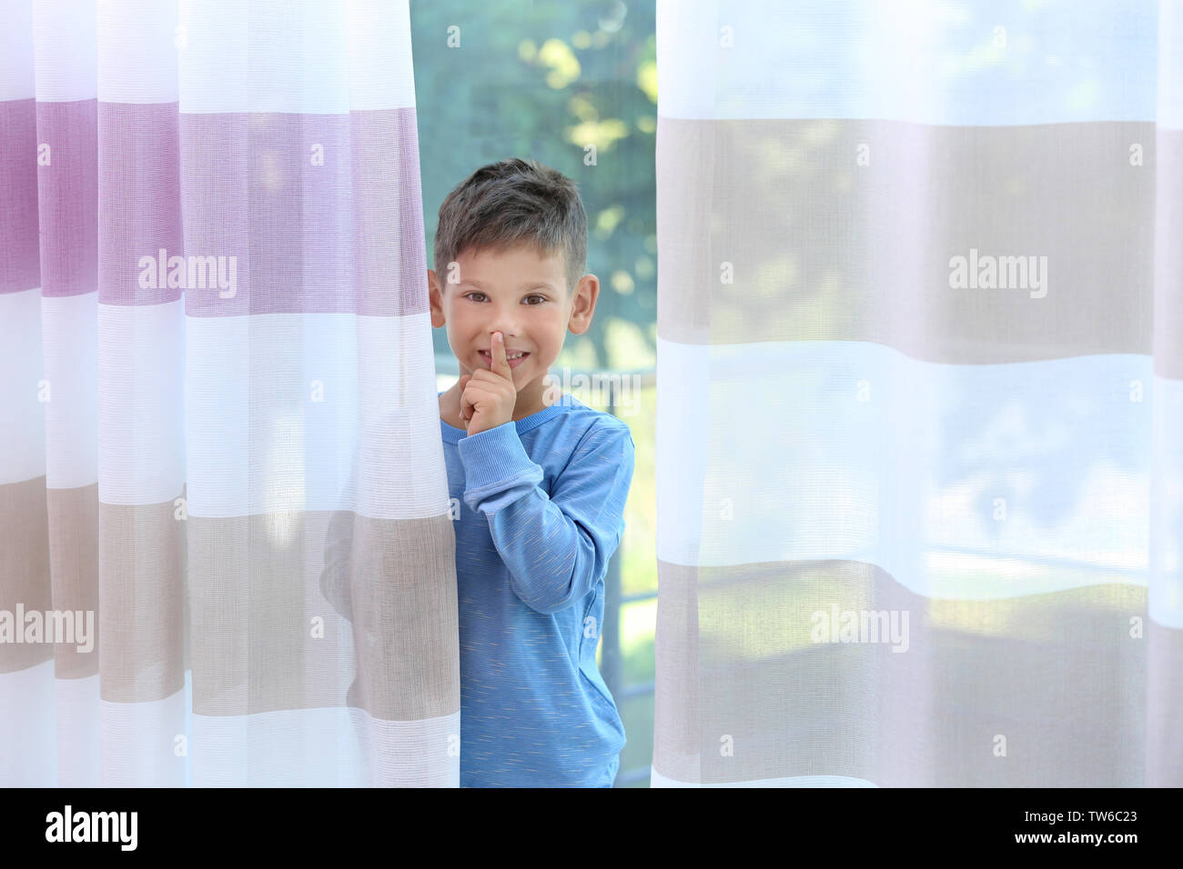 Cute little boy hiding behind curtains at home Stock Photo - Alamy