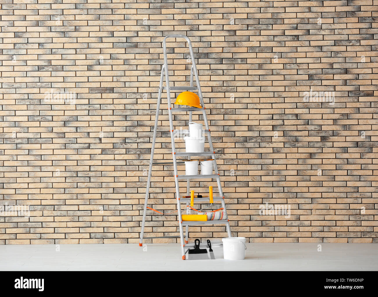 Composition with decorator's tools and paint on ladder near brick wall ...