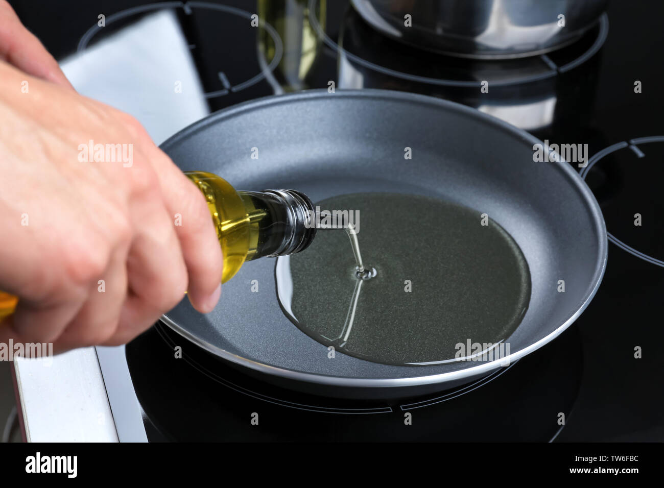 Man pouring cooking oil from bottle into frying pan on stove Stock ...