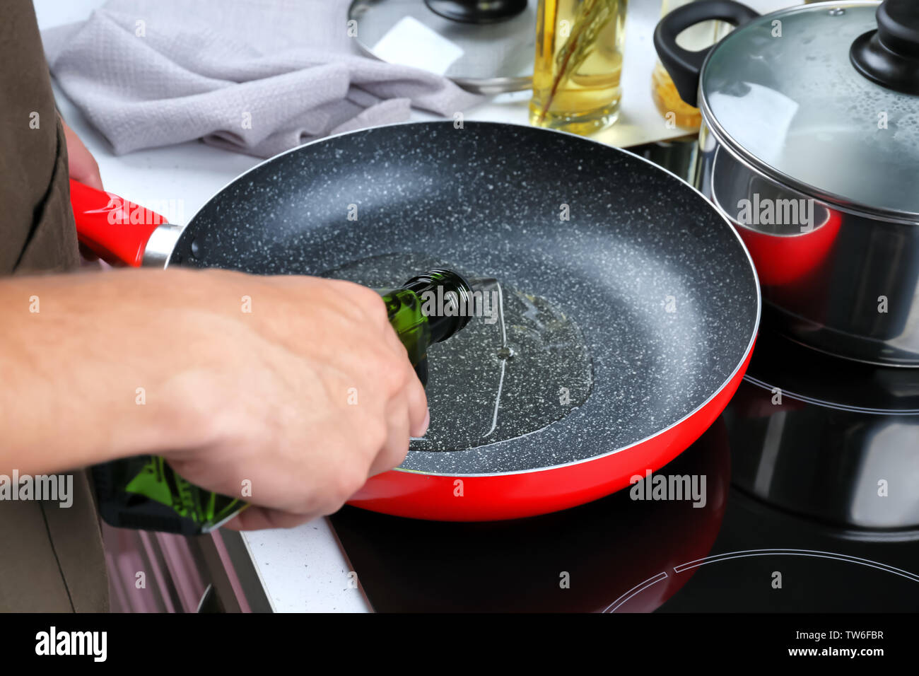 Man pouring cooking oil from bottle into frying pan on stove Stock ...