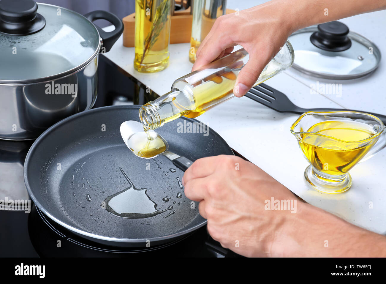 Man pouring cooking oil from bottle into spoon over frying pan in ...