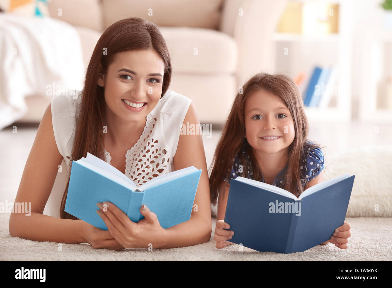 Young woman and her little daughter reading books at home Stock Photo ...