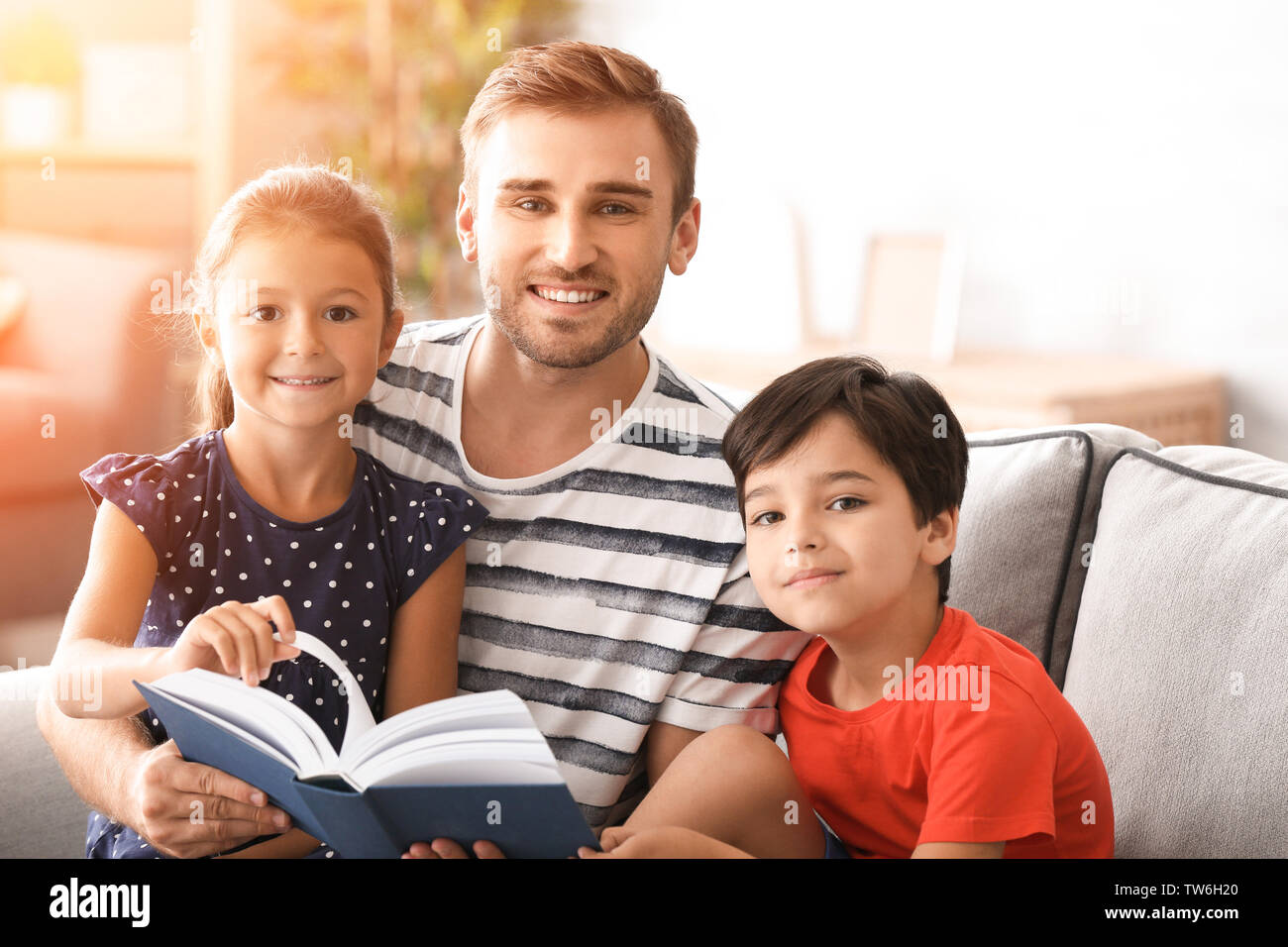 Young man and his little children reading book at home Stock Photo - Alamy