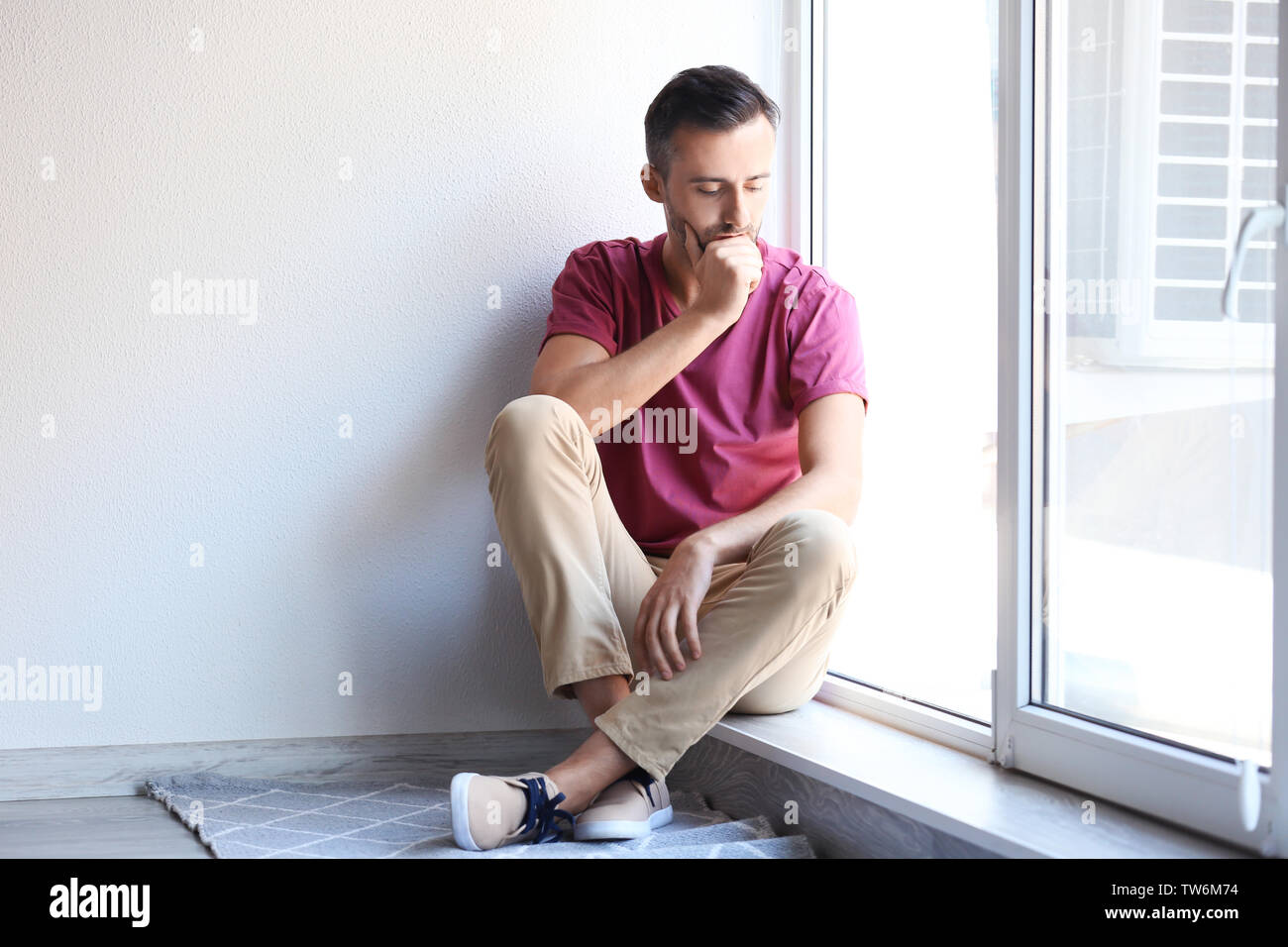 Depressed man sitting near window Stock Photo - Alamy