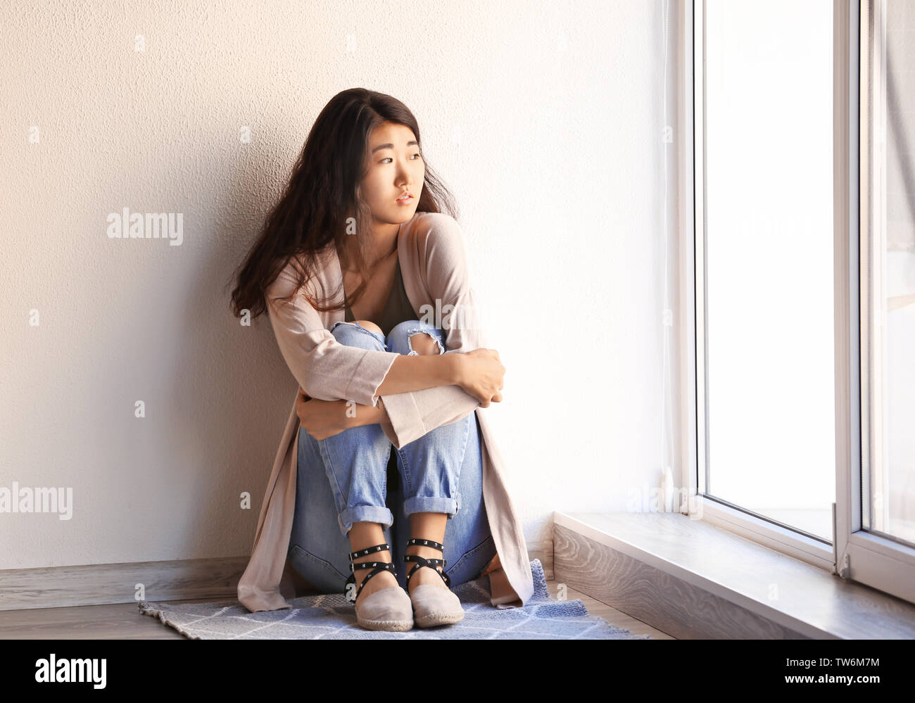 Sad young woman sitting near window Stock Photo - Alamy