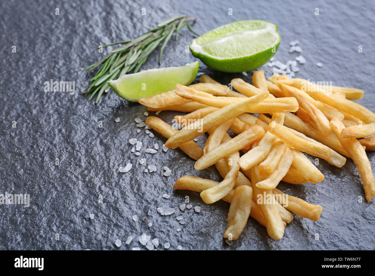 Yummy french fries with lime slices on dark texture background Stock ...