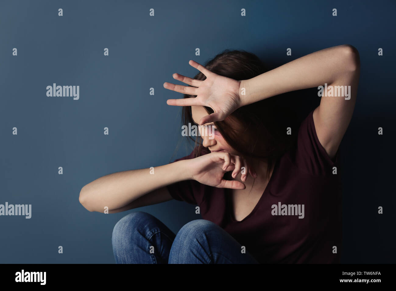 Battered young woman sitting on color background Stock Photo - Alamy