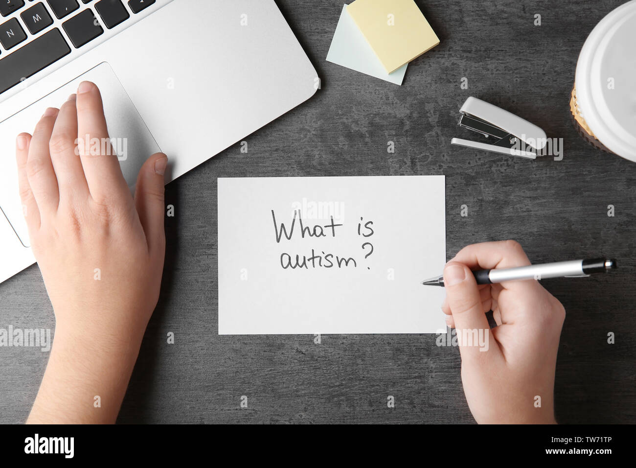 Woman writing "What is autism?" on sheet of paper at table Stock Photo ...