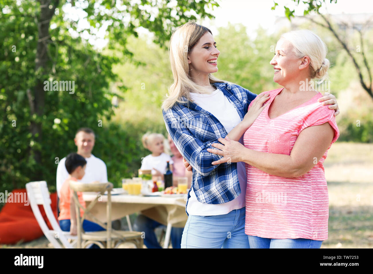 Happy mother and daughter with family having barbecue party outdoors ...
