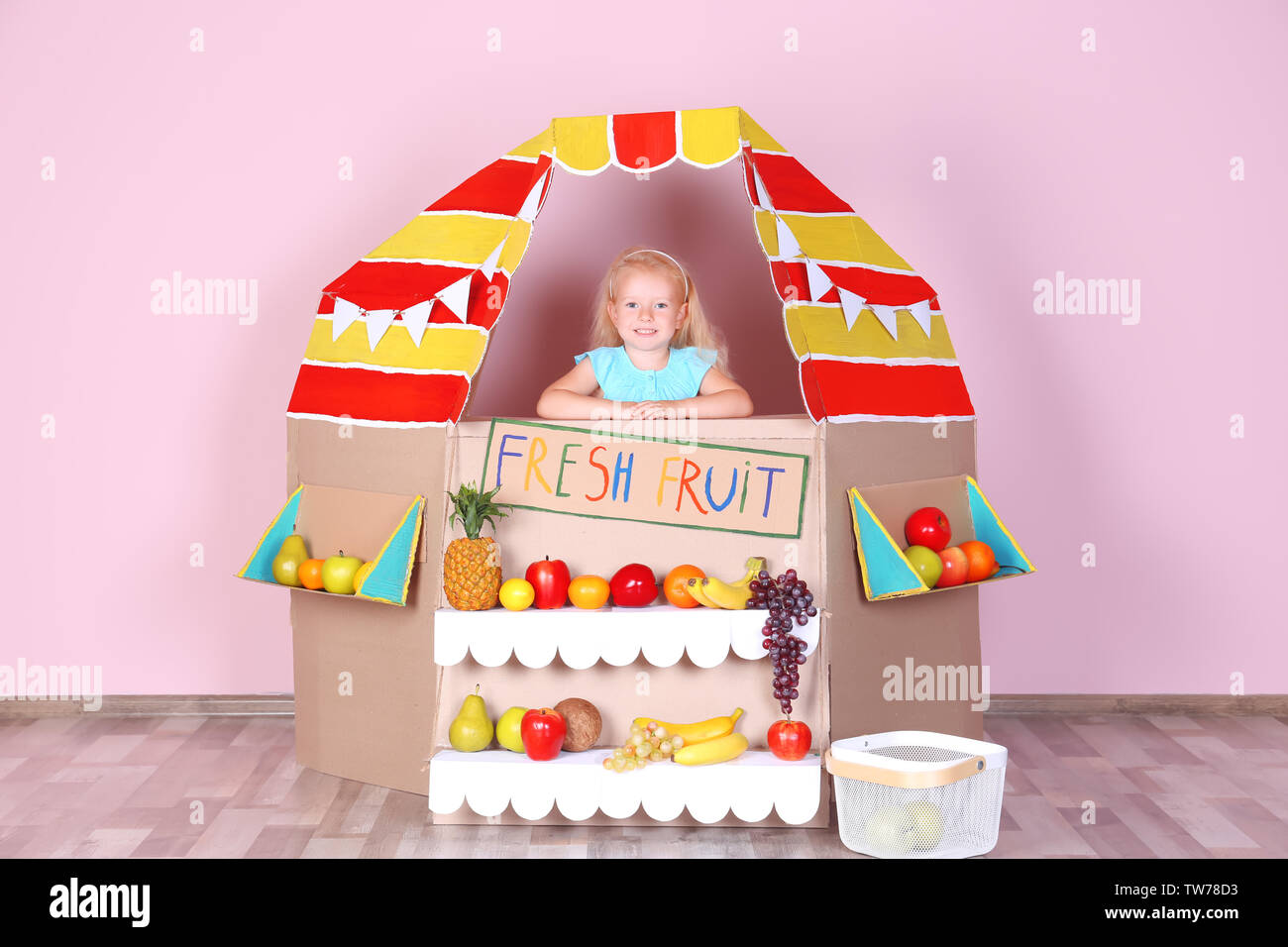 Little girl playing with cardboard stall on color wall background Stock ...