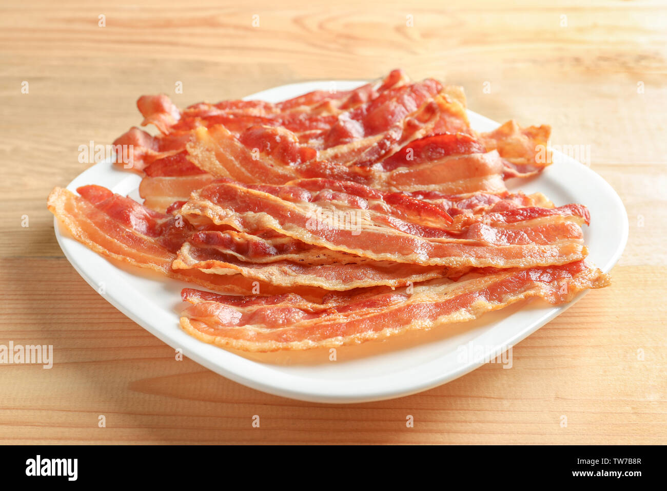 Plate with cooked bacon rashers on wooden table Stock Photo - Alamy