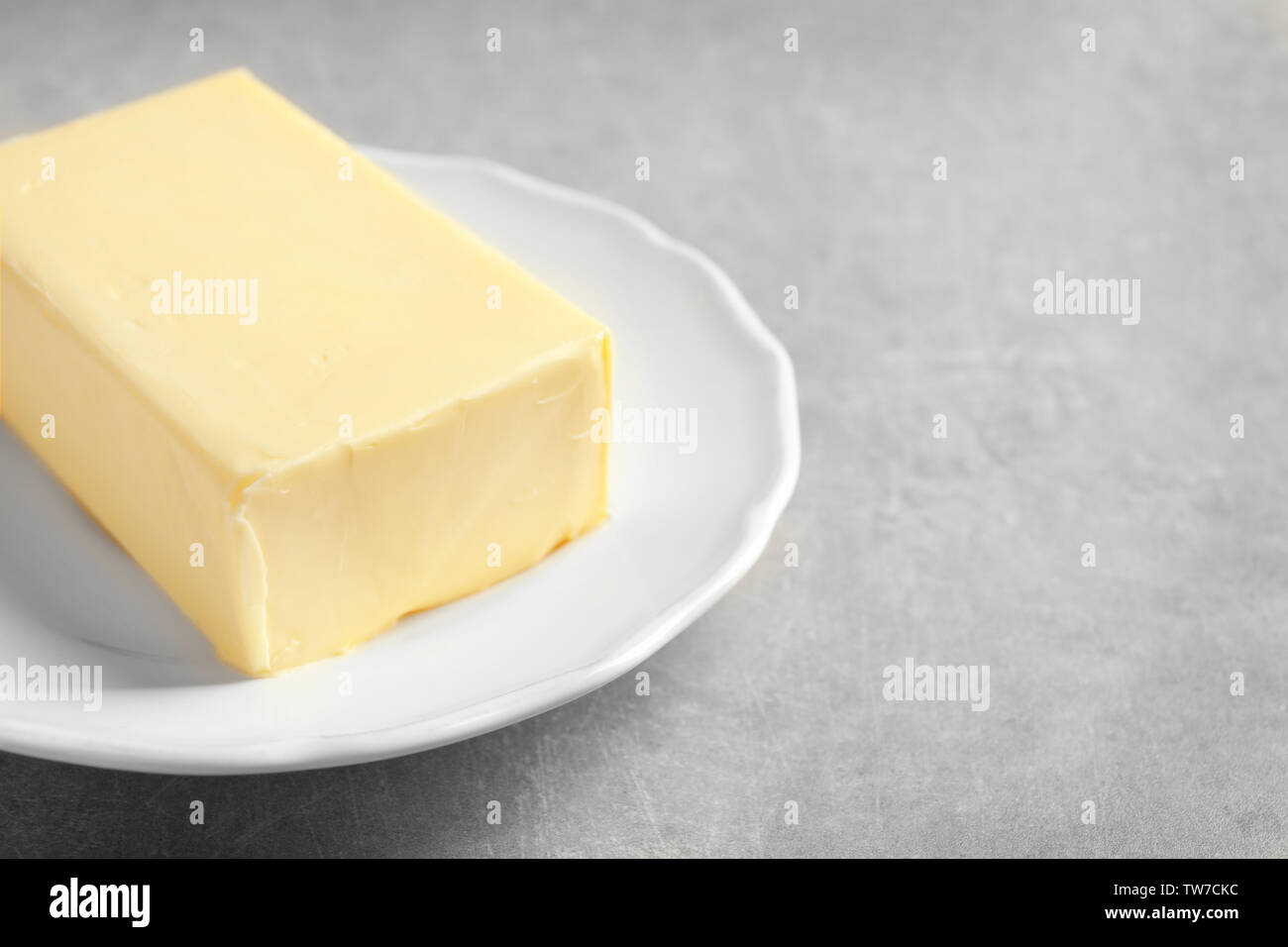 Plate with block of butter on grey background Stock Photo - Alamy
