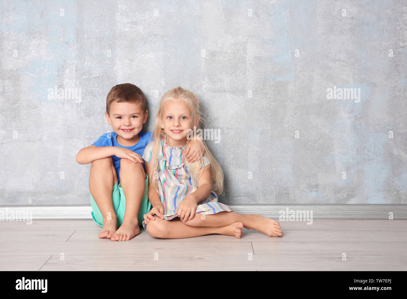 Cute little children sitting near grey wall Stock Photo - Alamy