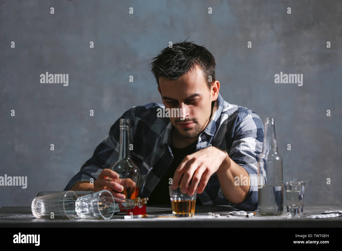 Drunk man sitting at table with alcohol and drugs. Alcoholism concept ...