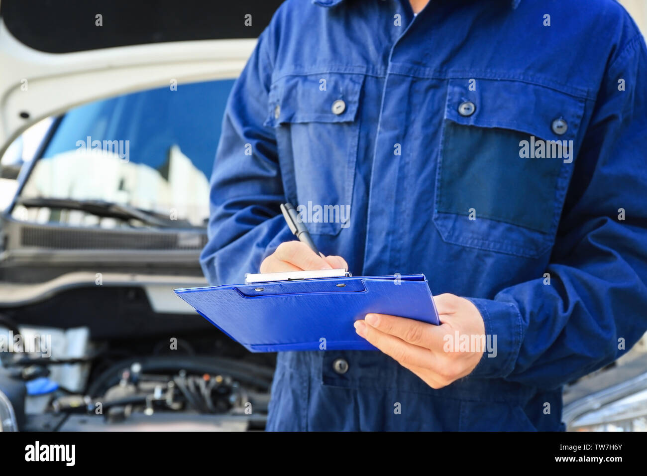 Auto mechanic with clipboard near car, closeup Stock Photo - Alamy
