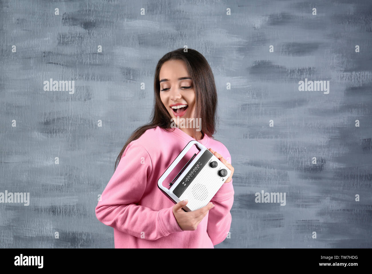 Young woman listening to radio against grey background Stock Photo - Alamy