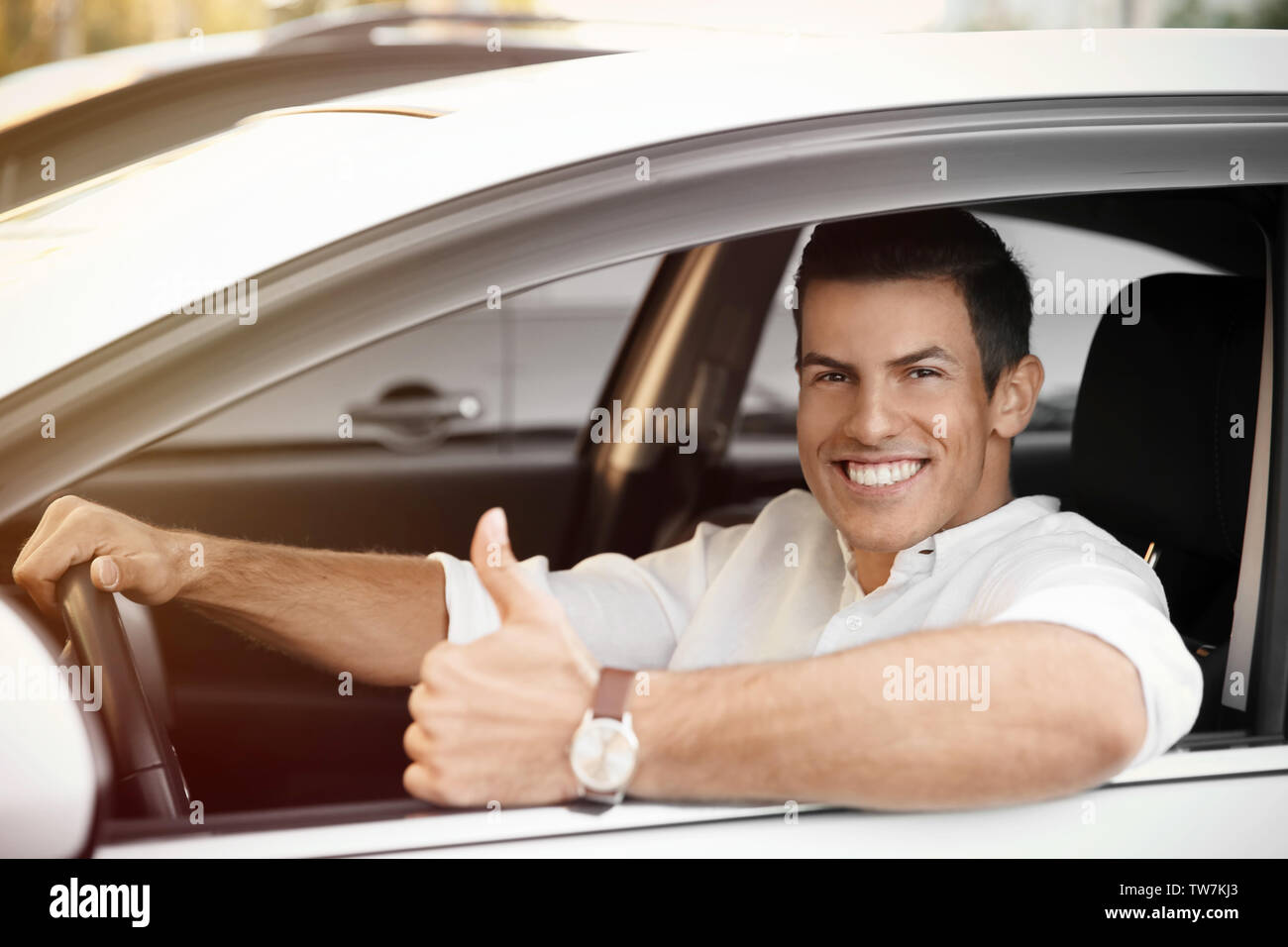 Young man showing thumb up gesture while sitting on driver seat of car ...
