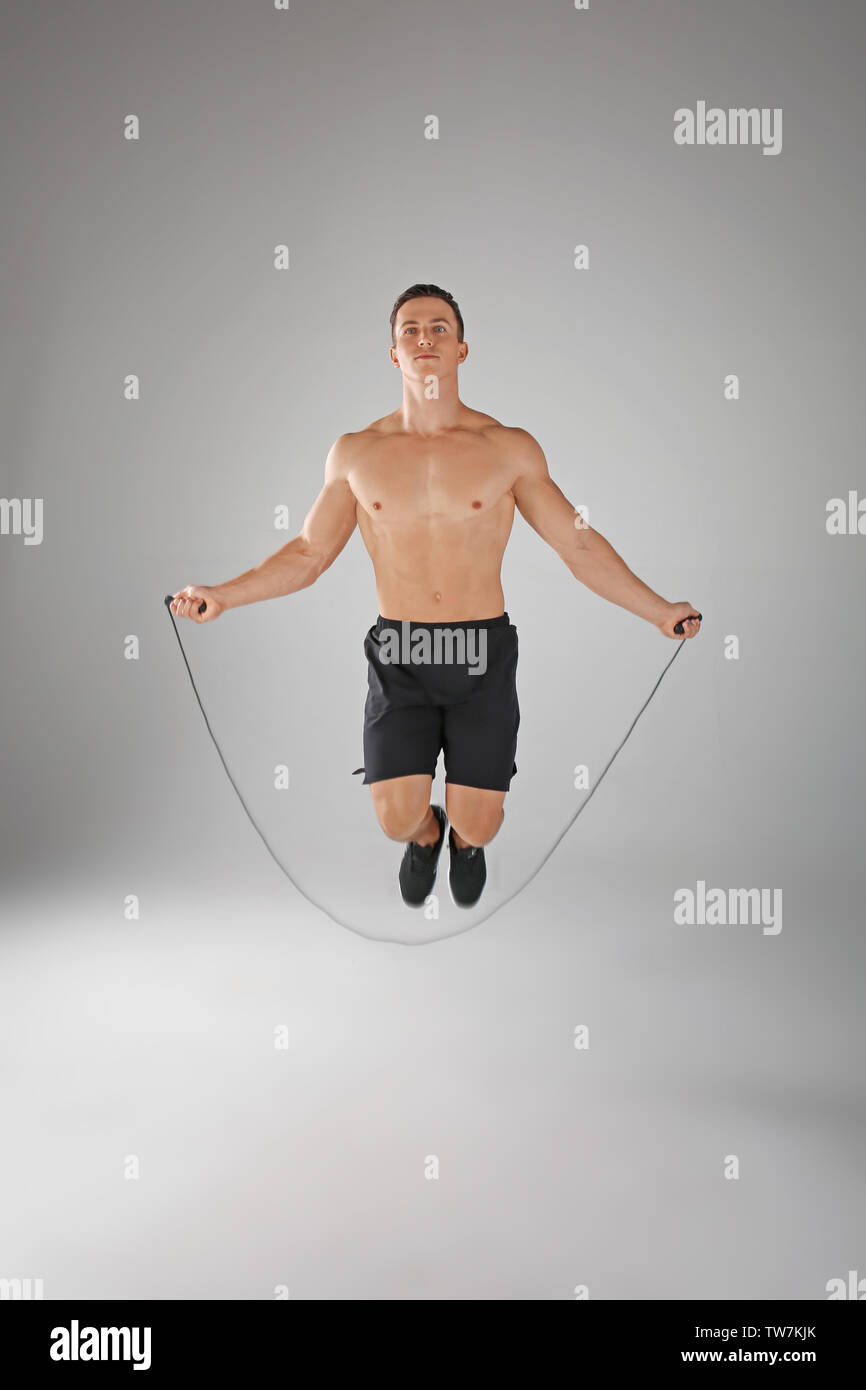 Sporty young man jumping rope on grey background Stock Photo - Alamy