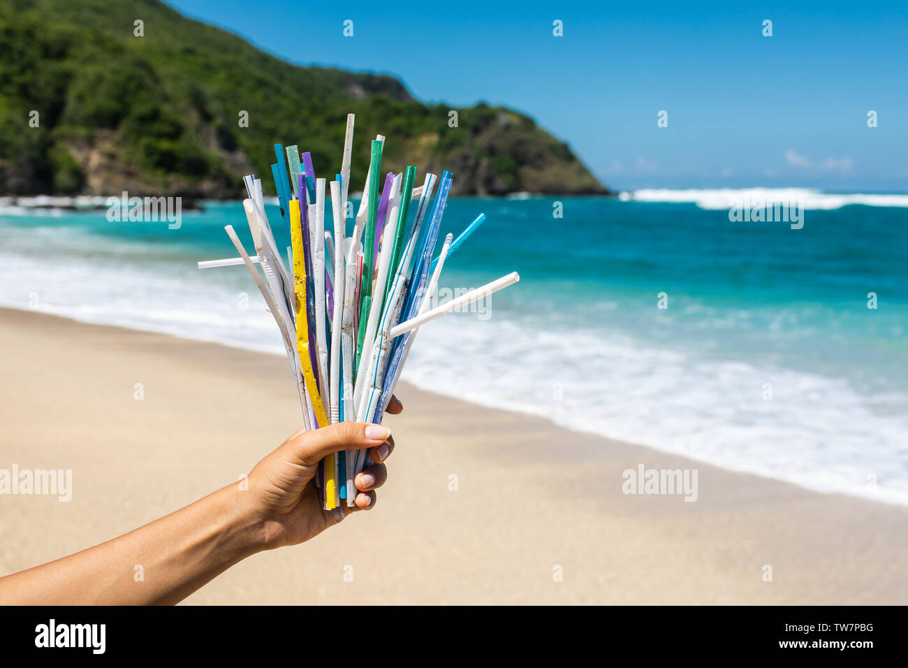 Hand holding heap of used plastic straws on background of clean beach ...