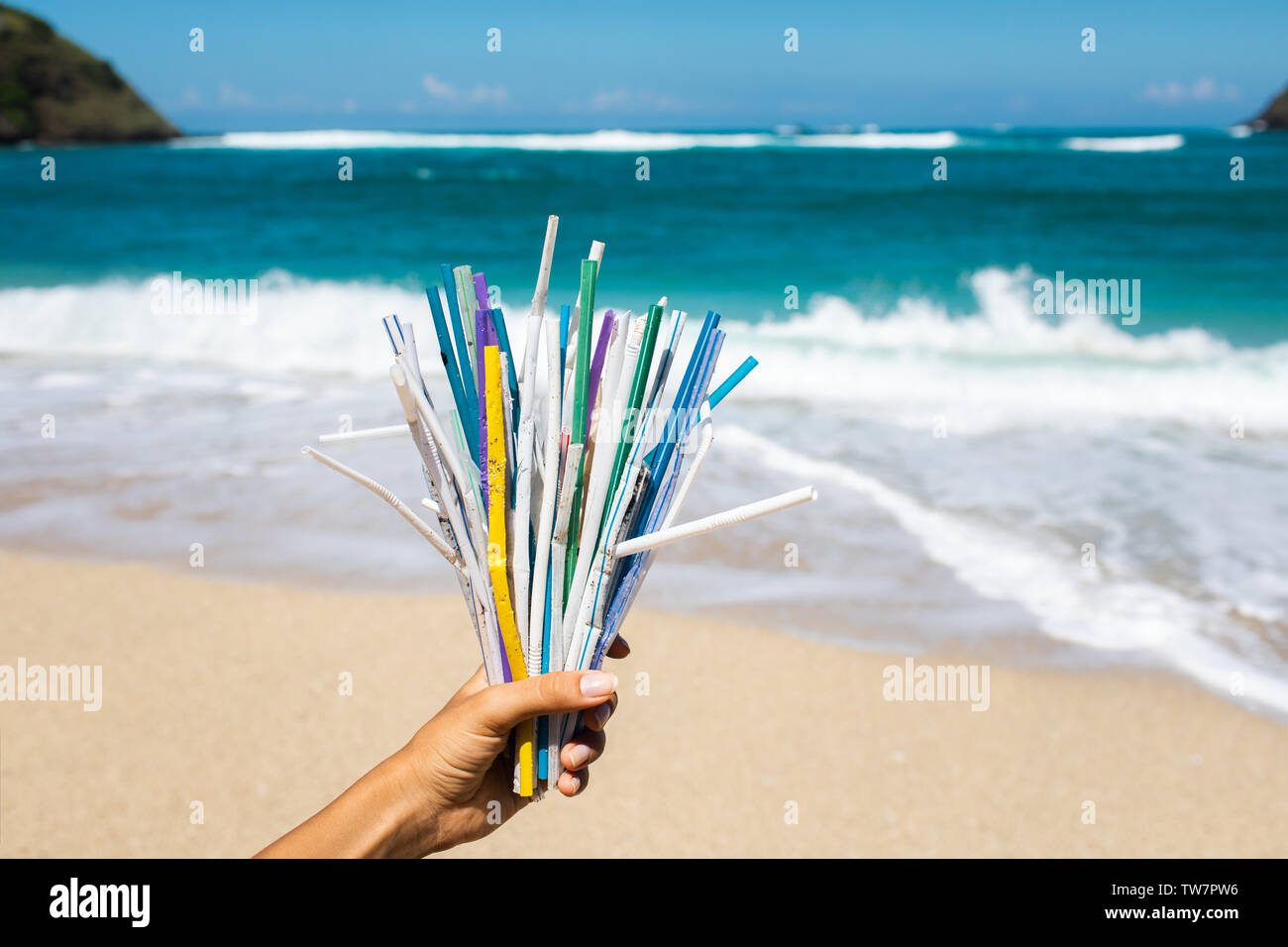 Hand holding heap of used plastic straws on background of clean beach ...