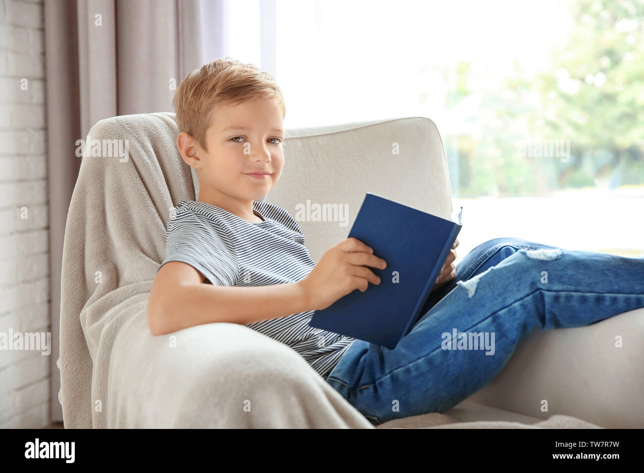 Cute little boy reading in armchair at home Stock Photo - Alamy