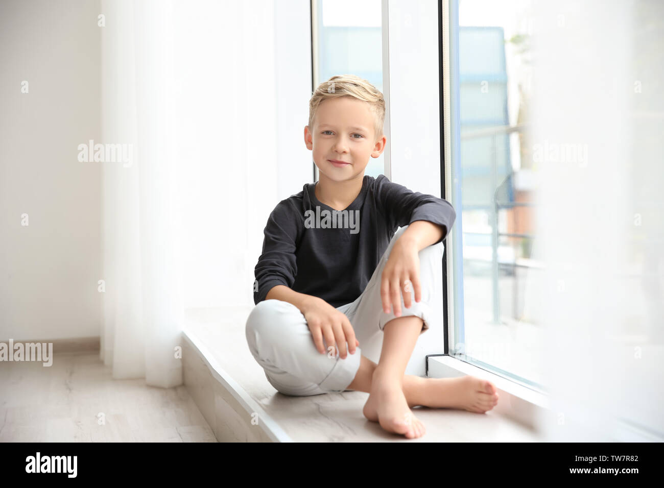 Cute little boy sitting near window at home Stock Photo - Alamy