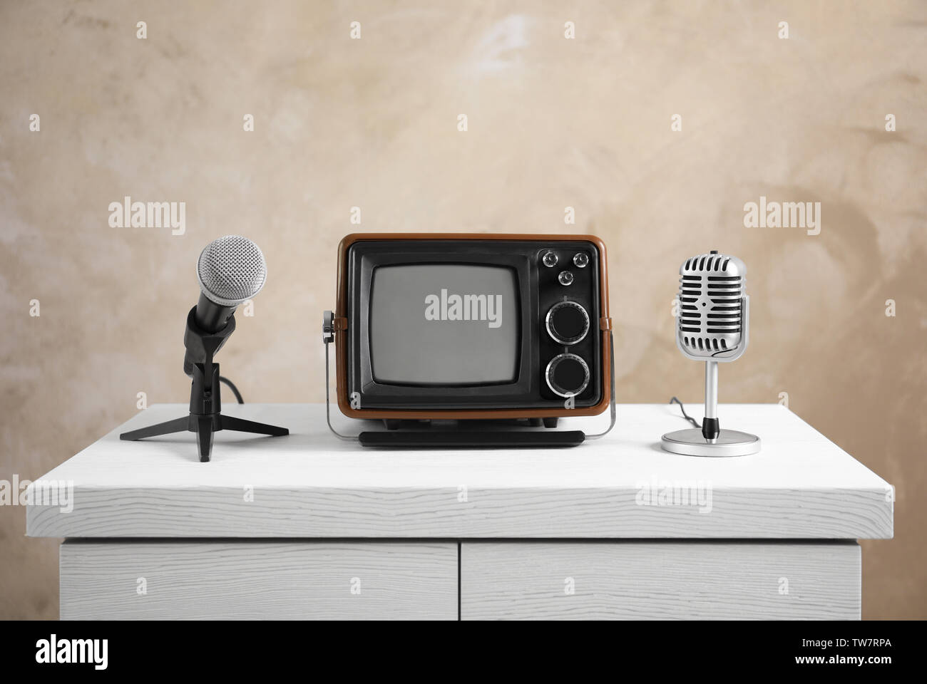 Retro portable TV and microphones on table against light wall Stock ...