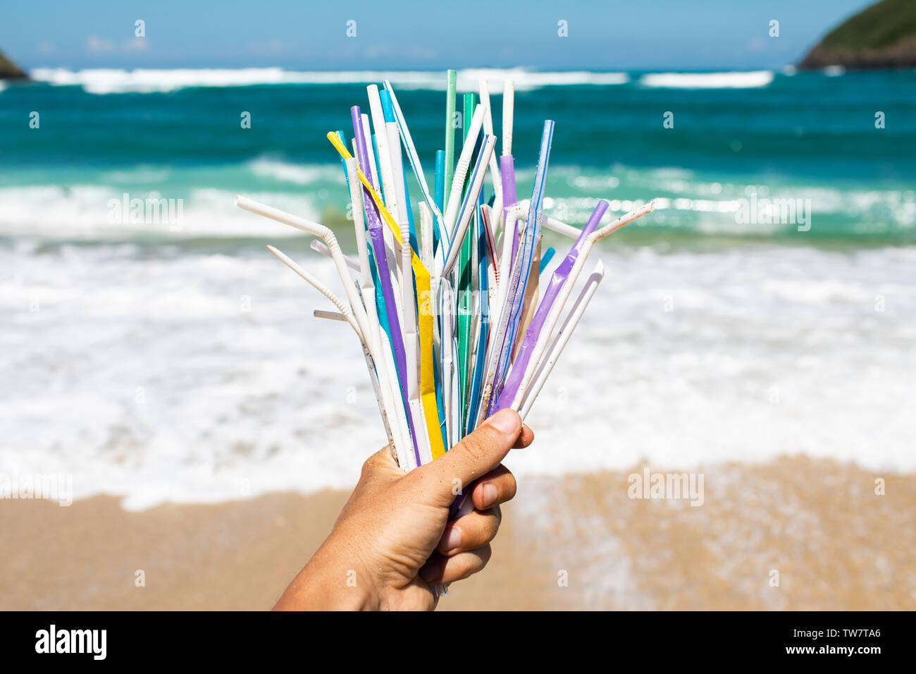 Hand holding heap of used plastic straws on background of clean beach ...