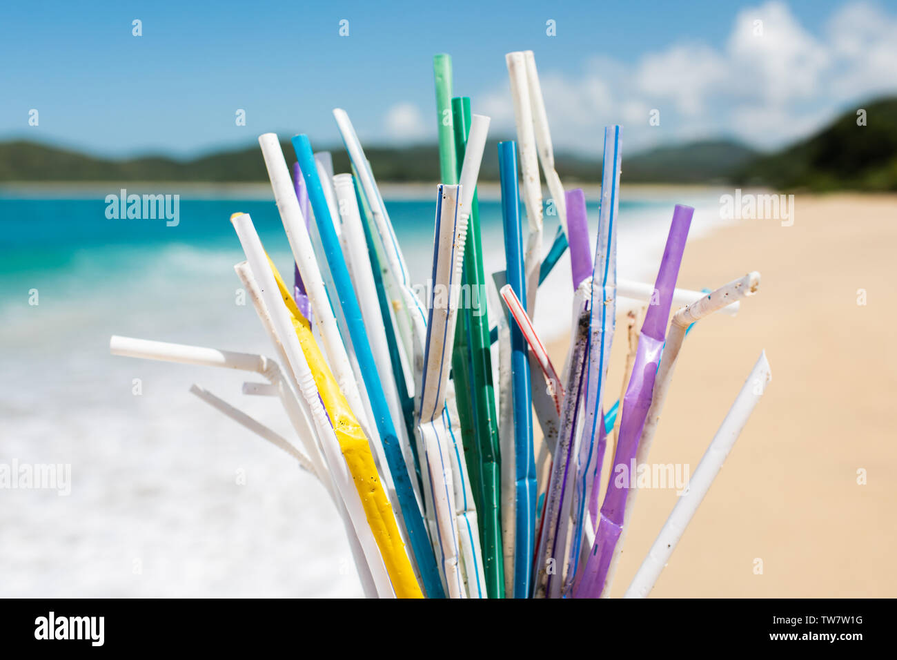 Heap of used plastic straws on background of clean beach and ocean ...
