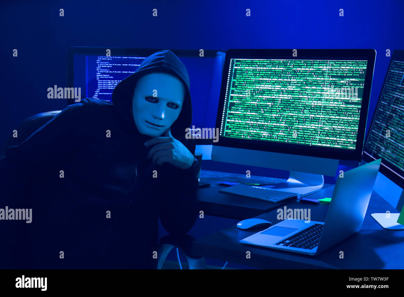 Hacker in mask using computer in dark room Stock Photo - Alamy