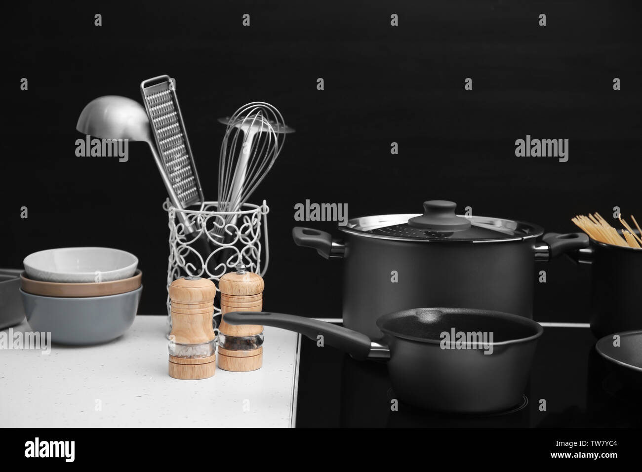Different cooking utensils on electric stove against black background ...