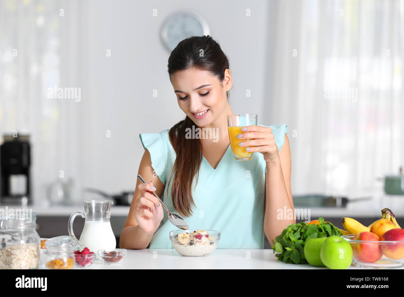 Young woman eating oatmeal at table in kitchen Stock Photo - Alamy