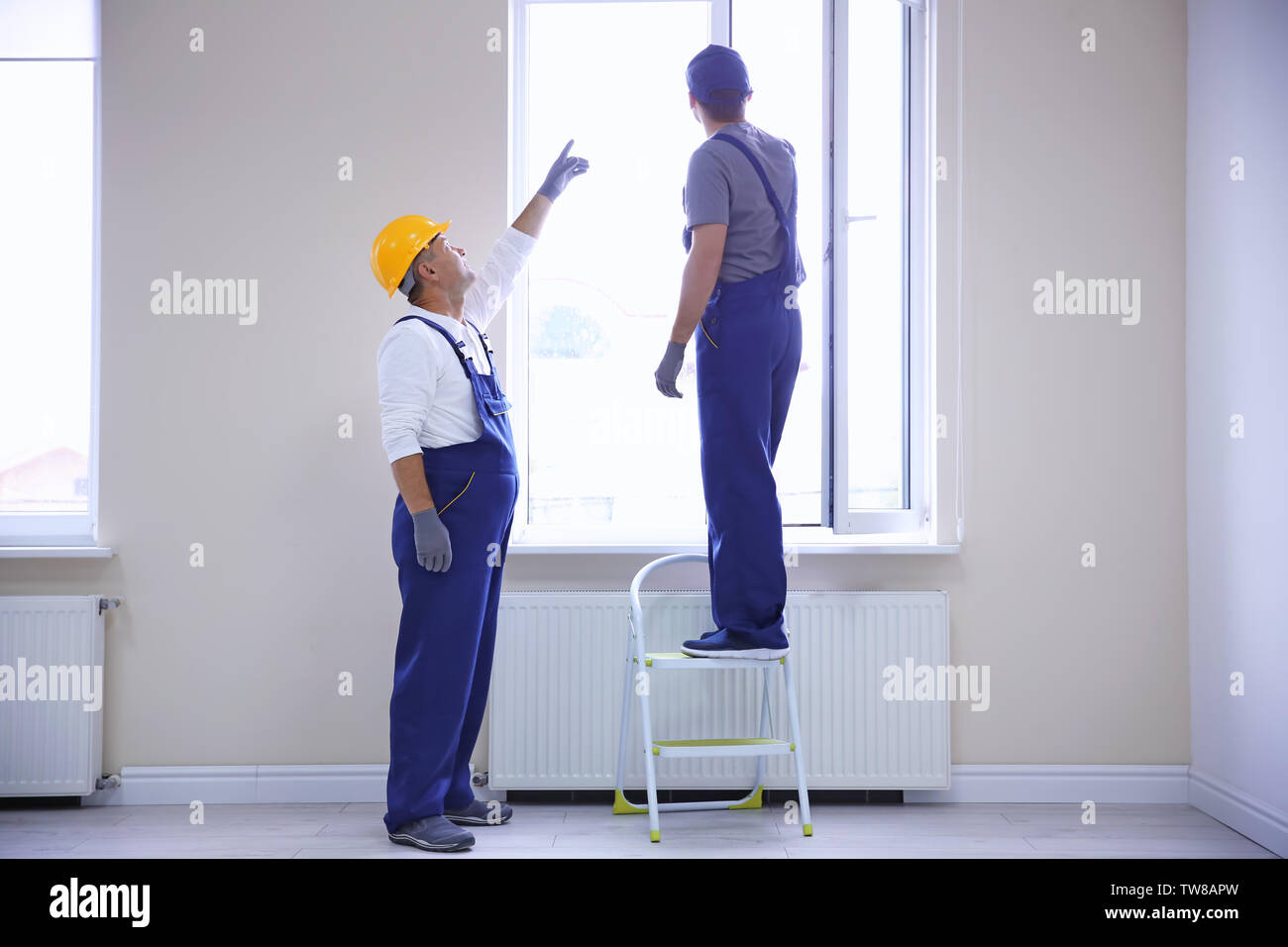 Construction worker with trainee installing window in house Stock Photo ...