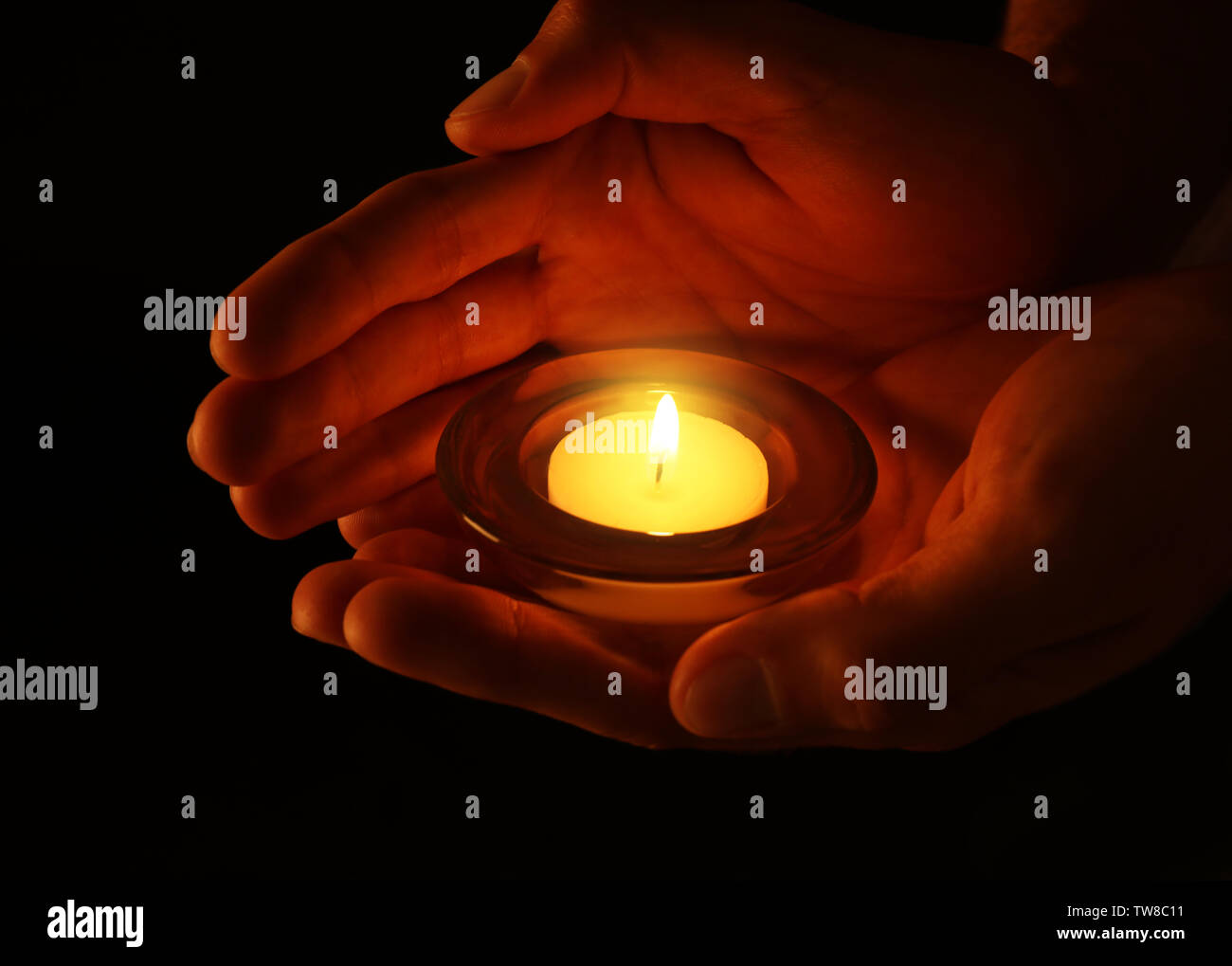 Young man holding burning candle in darkness Stock Photo - Alamy