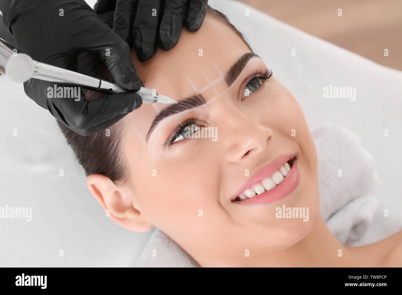 Young woman undergoing procedure of eyebrow permanent makeup in beauty ...