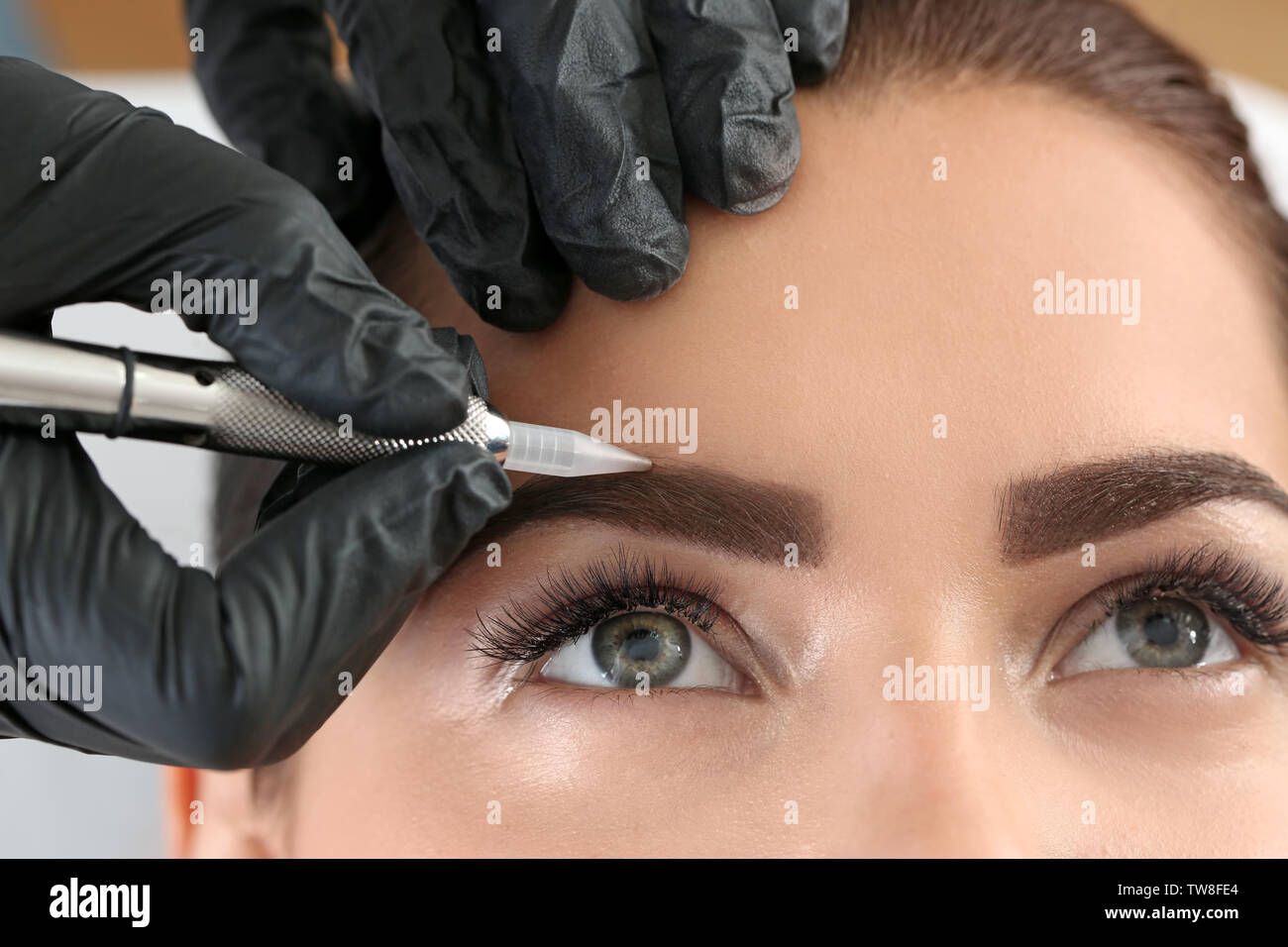 Young woman undergoing procedure of eyebrow permanent makeup in beauty ...