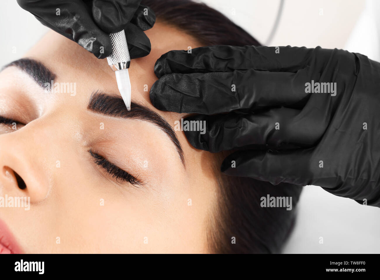 Young woman undergoing procedure of eyebrow permanent makeup in beauty ...