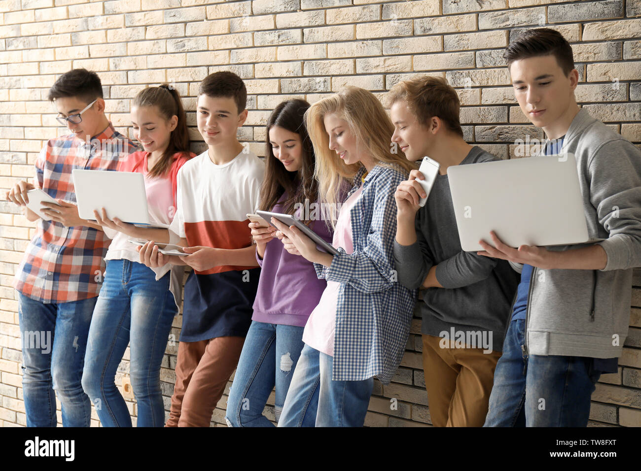 Group of cool teenagers with modern devices near brick wall Stock Photo ...