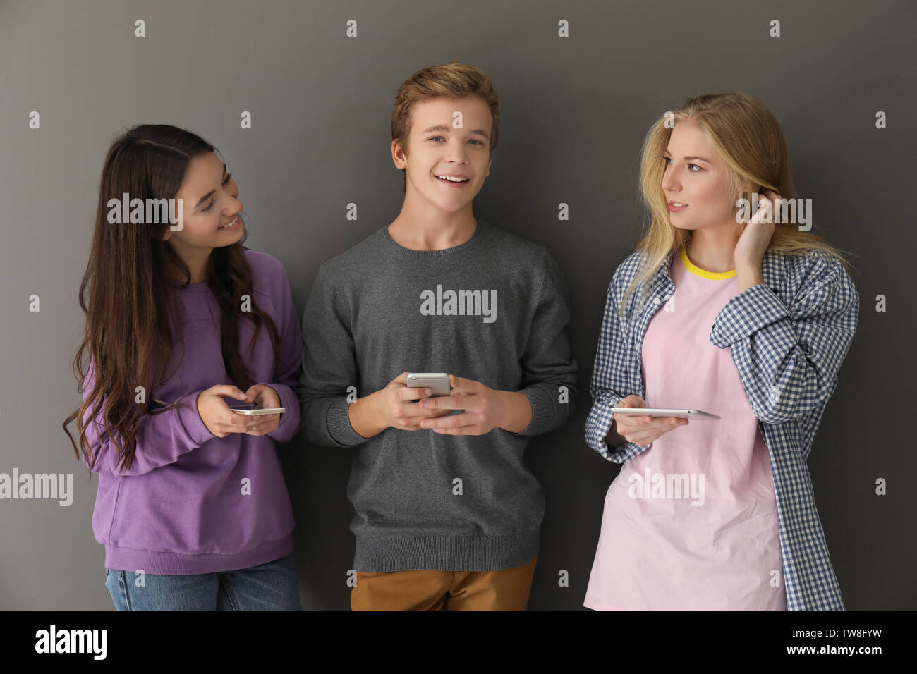 Cool teenagers with modern devices on grey background Stock Photo - Alamy